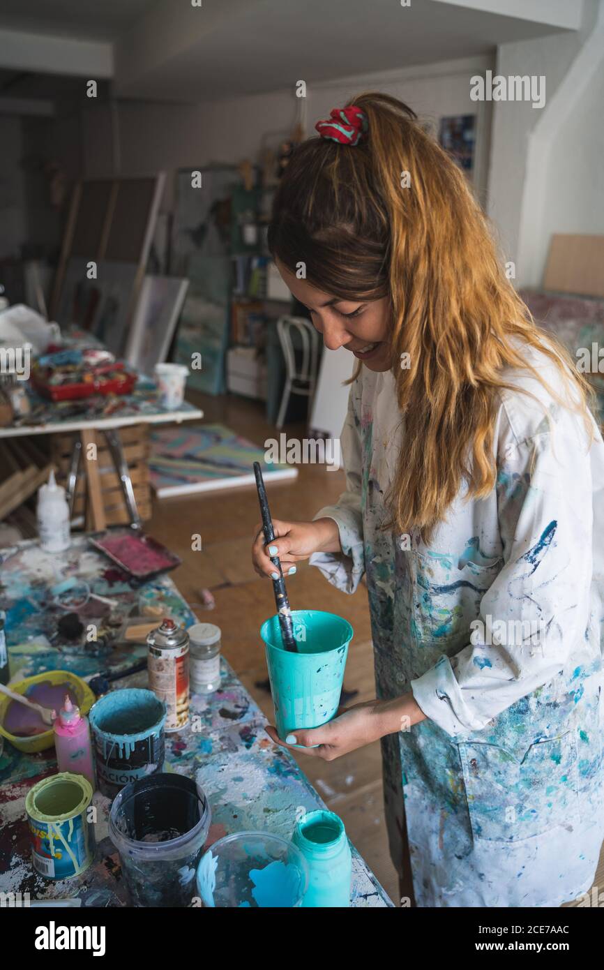 Side view young female artist standing at counter with various tools ...