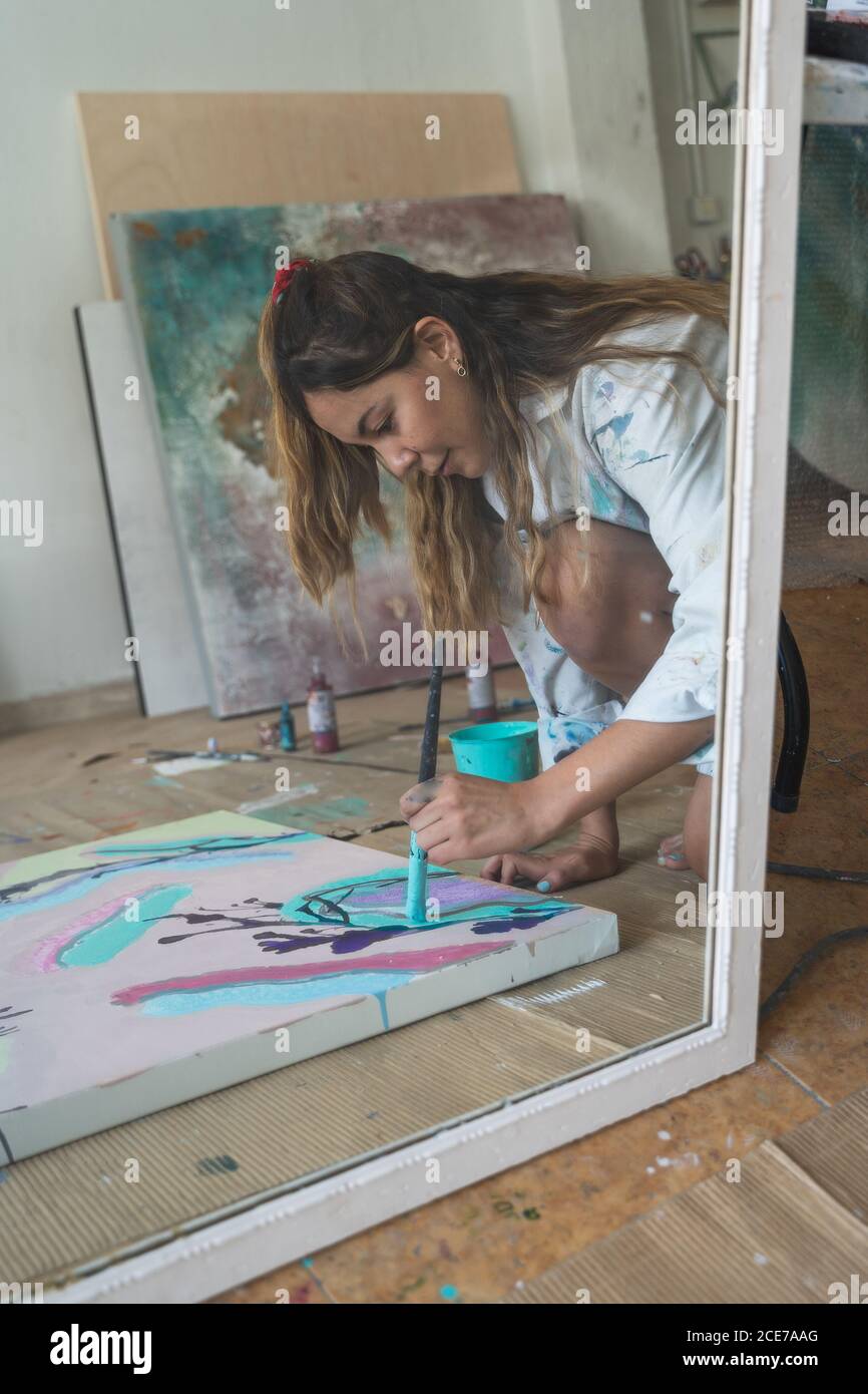 Side view of young female artist reflected in mirror painting creative ...