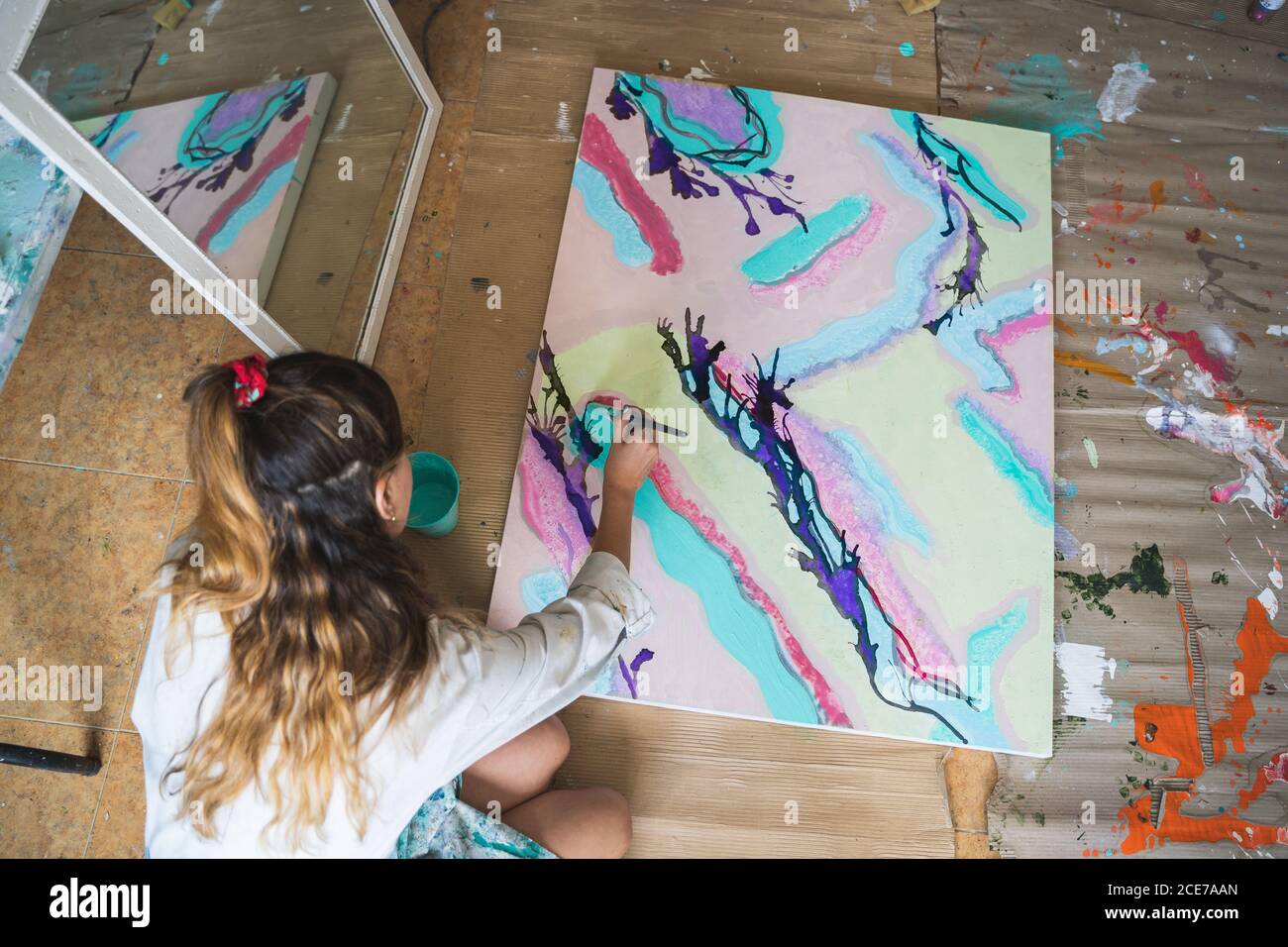 Cheerful barefoot female artist in dirty robe and gloves lying on ...