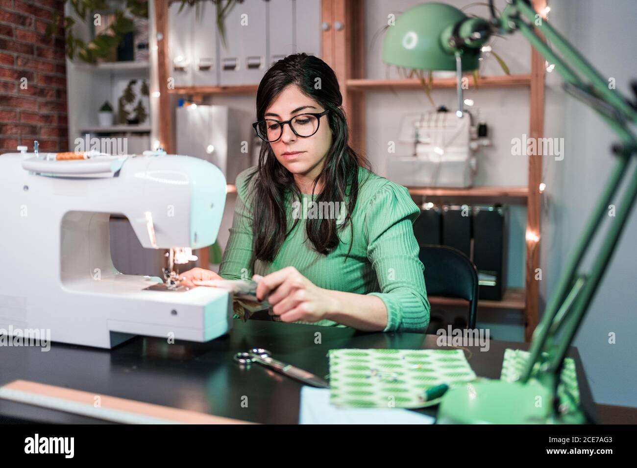 Slim female tailor in casual wear using sewing machine while sitting in ...