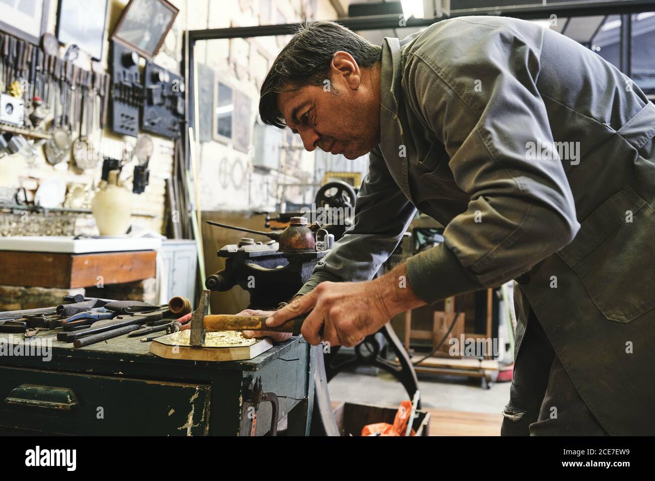 Crop male goldsmith hitting metal detail with hammer during work in ...