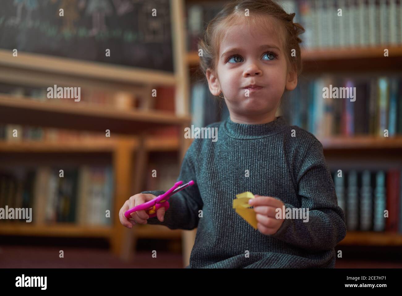 Cute little caucasian girl is playing with scissors and colored paper ...