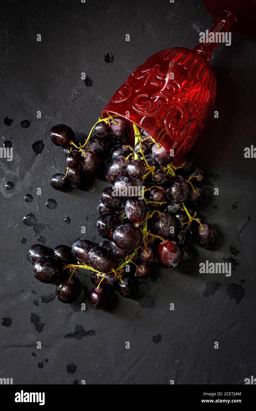 Top view of ripe juicy red grapes spilled from red wine goblet on black ...