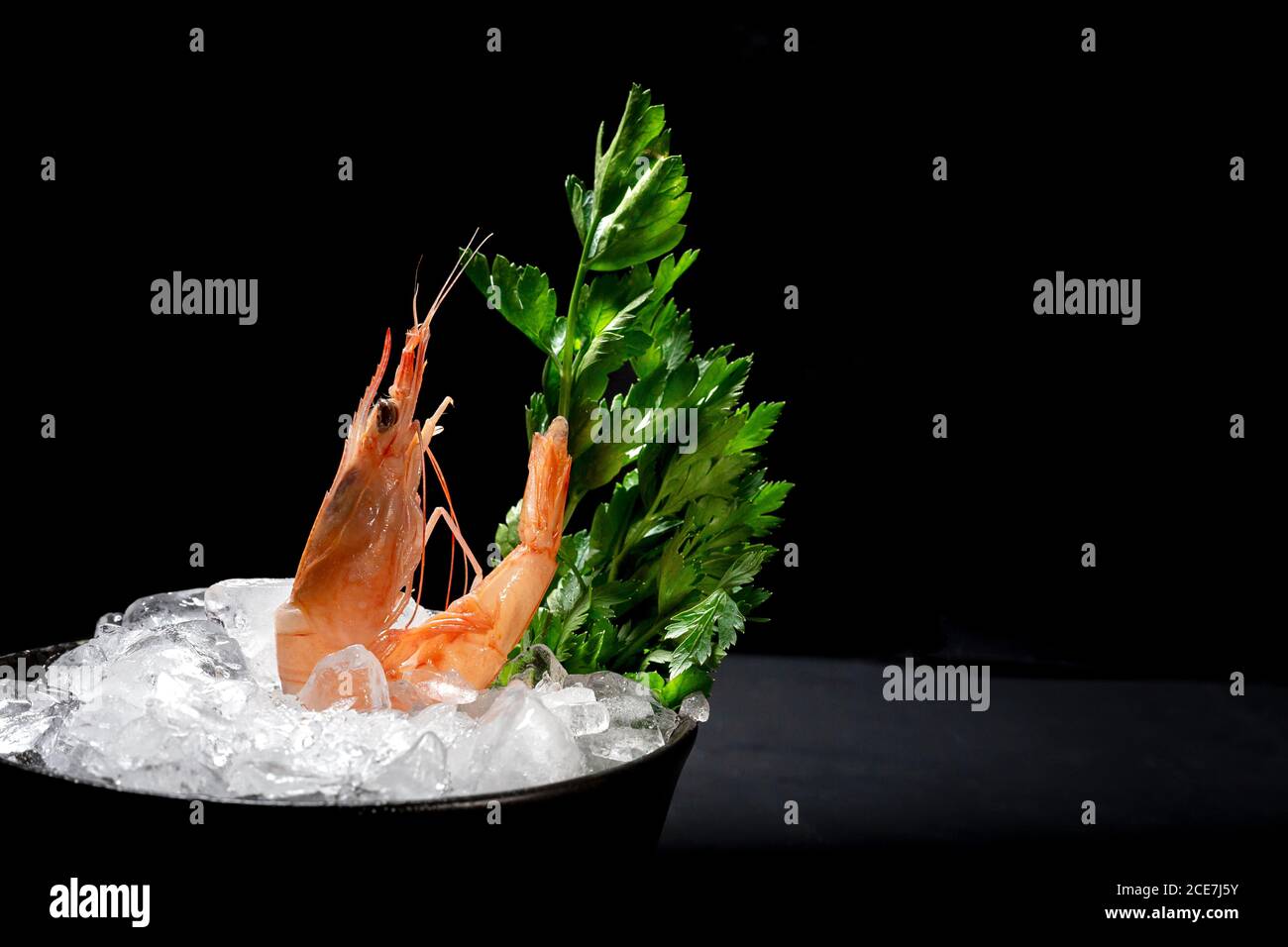 High angle of prawn in bowl with ice and parsley placed on black table ...