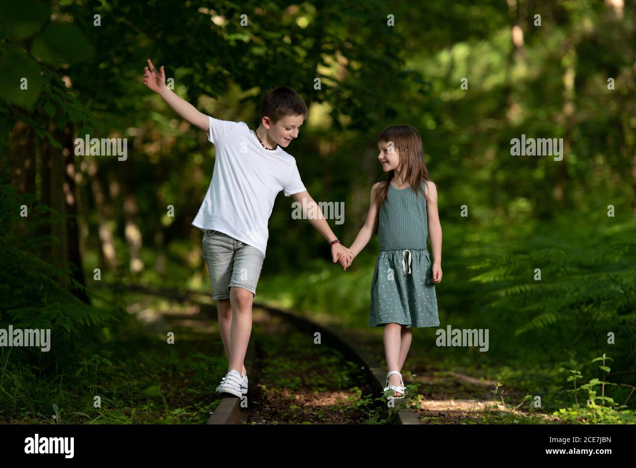 Friendly brother and sister smiling and walking along abandoned rails ...