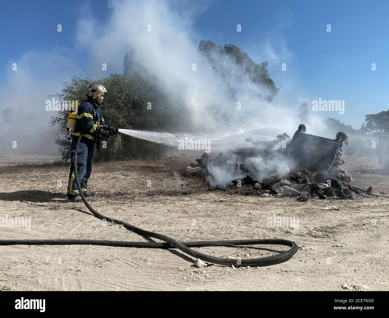 Side view of brave fireman in protective uniform standing with hose and ...