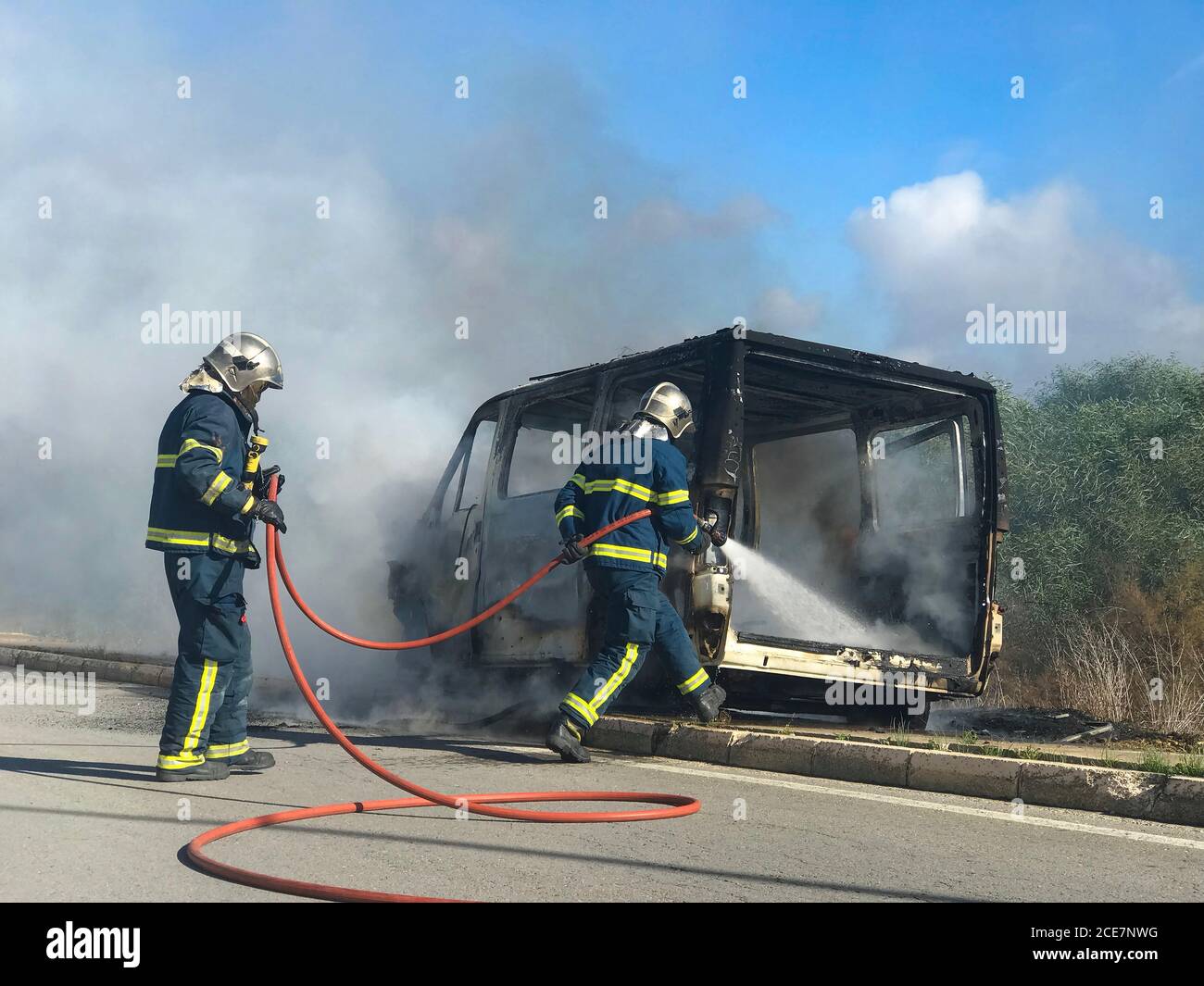 Low angle back view of firefighters extinguishing fire with water hose ...