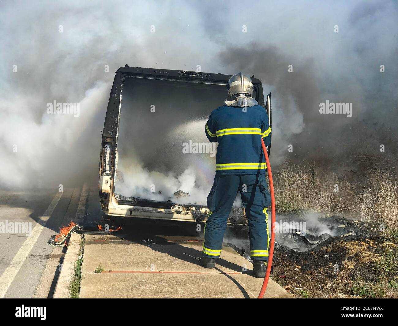 Low angle back view of firefighter extinguishing fire with water hose ...