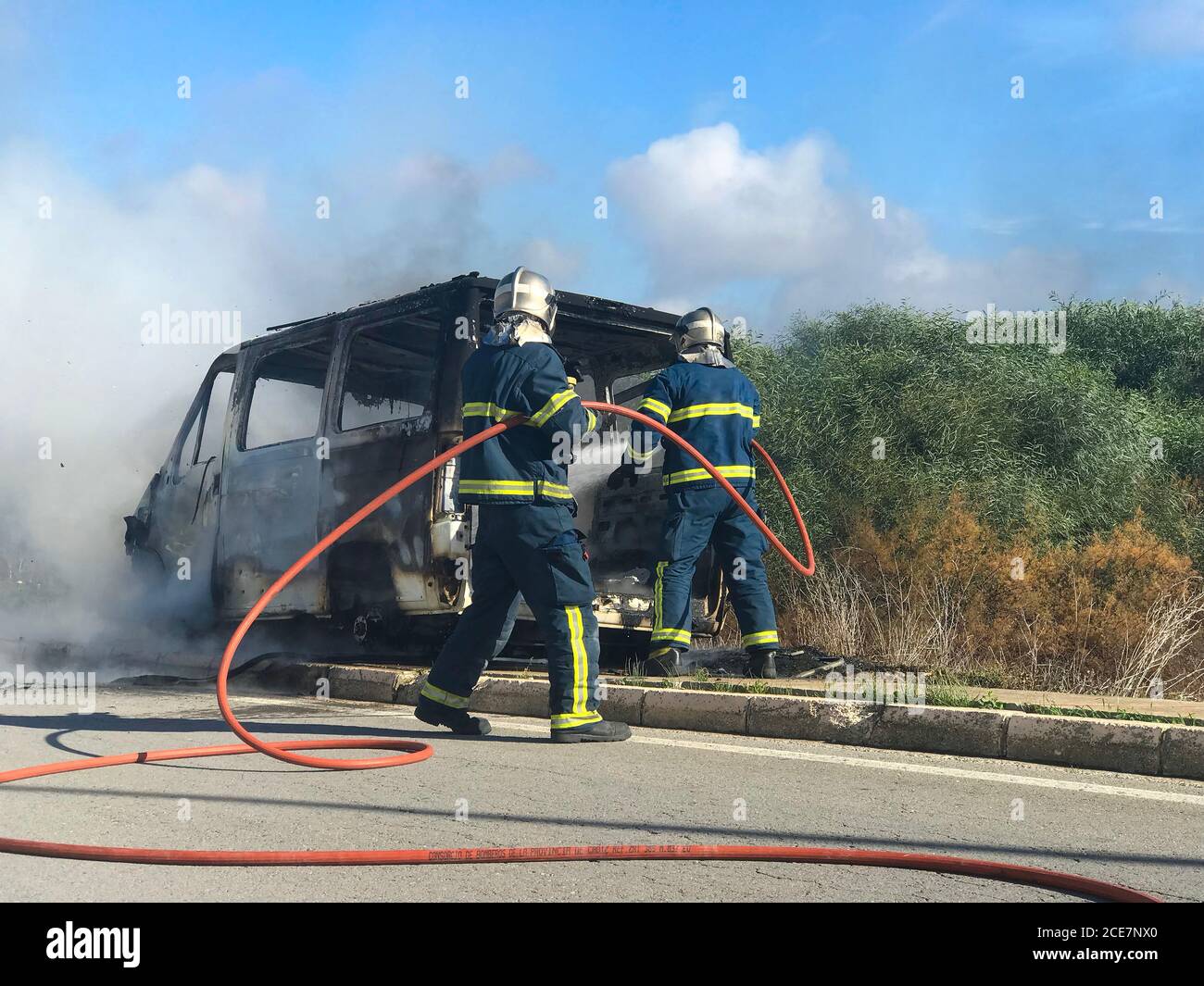 Low angle back view of firefighters extinguishing fire with water hose ...