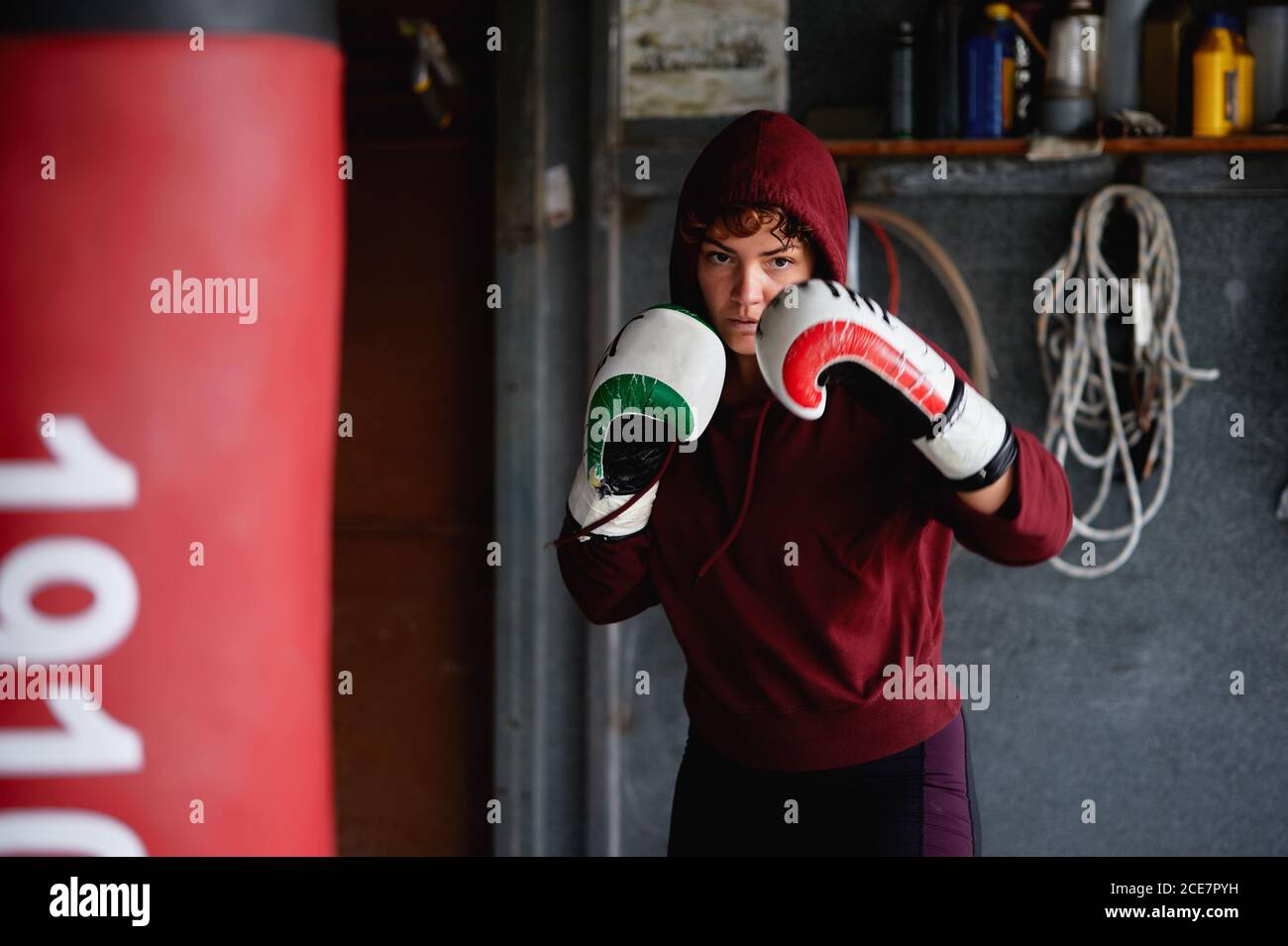 Strong female boxer wearing dark red hoodie and boxing gloves shadows ...