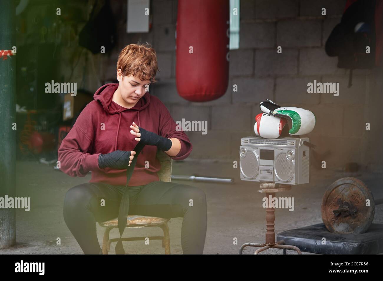 Crop concentrated female boxer in leggings and hoodie wrapping hands ...