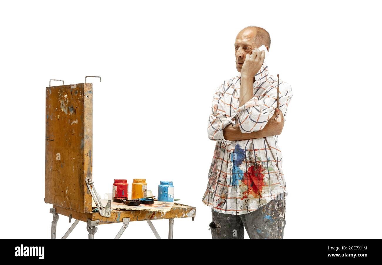 Talking phone. Male caucasian artist, painter at work on white studio ...