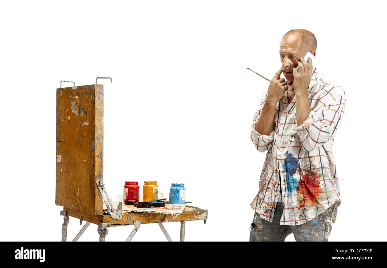 Talking phone. Male caucasian artist, painter at work on white studio ...