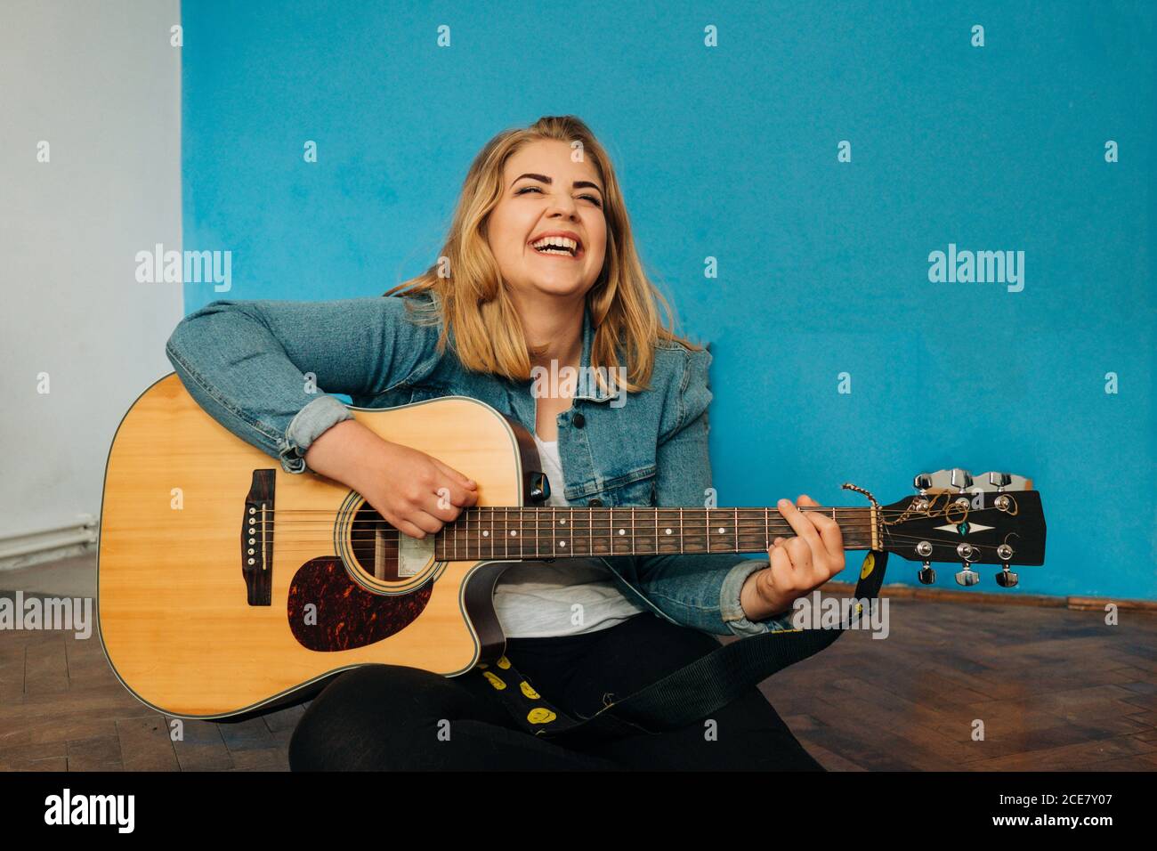 Young cheerful female musician laughing and playing acoustic guitar ...