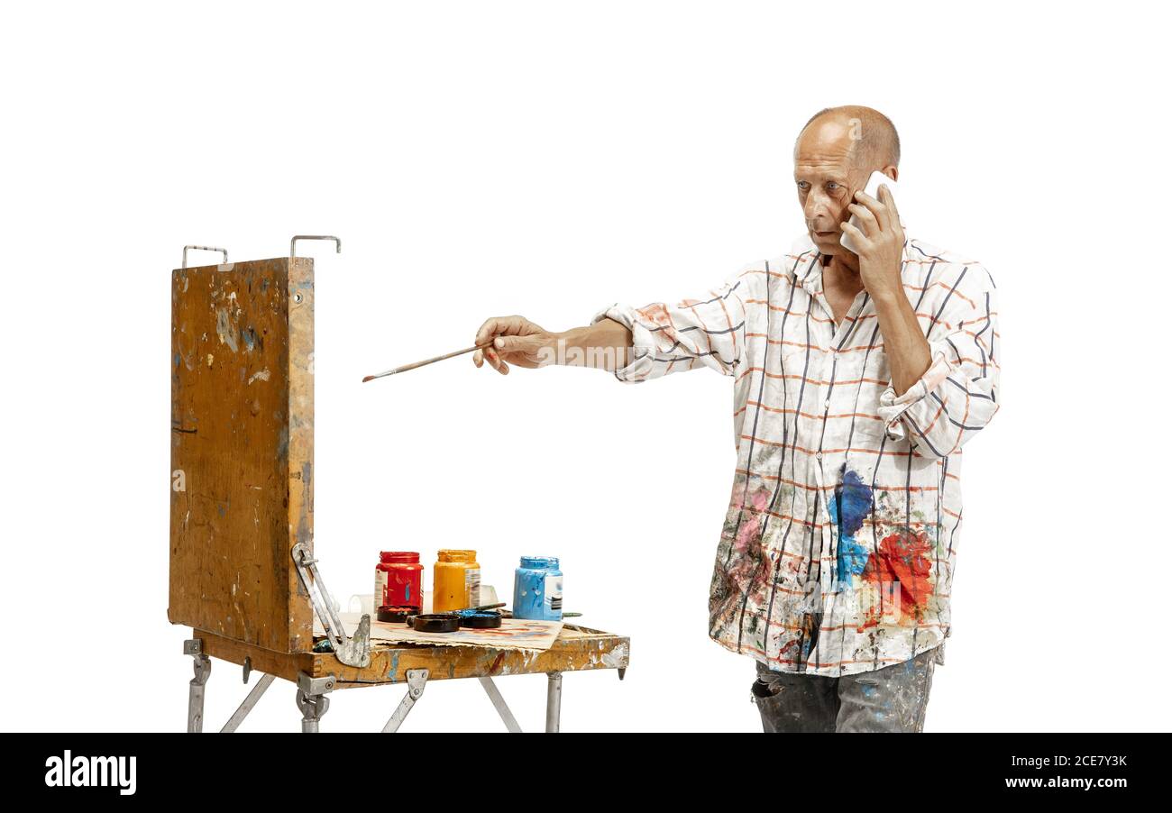 Talking phone. Male caucasian artist, painter at work on white studio ...