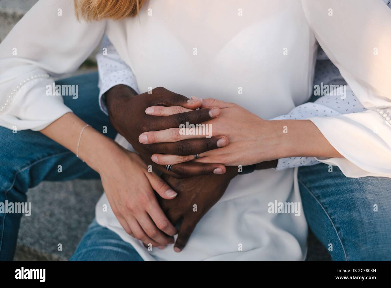 Crop faceless multiethnic couple bonding and holding hands together ...