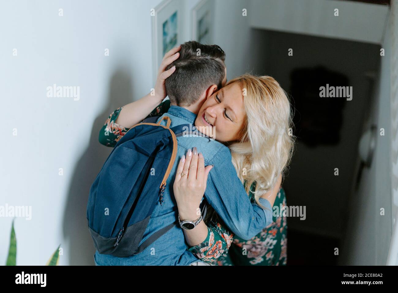 Content mother gently kissing teenage son with school backpack while ...