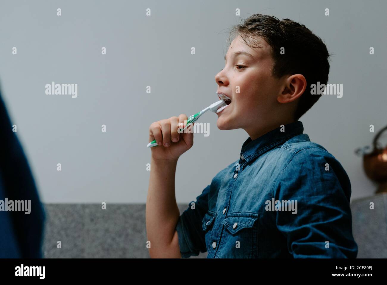 Side view adorable positive boy in denim shirt brushing teeth with ...