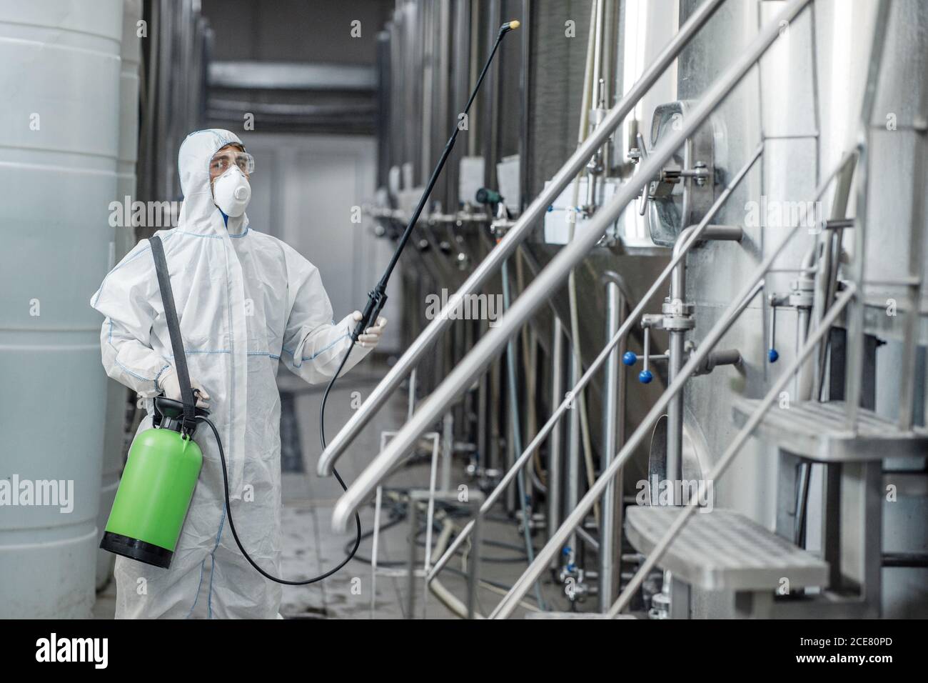 Factory worker in protective suit with spray bags disinfects plant ...