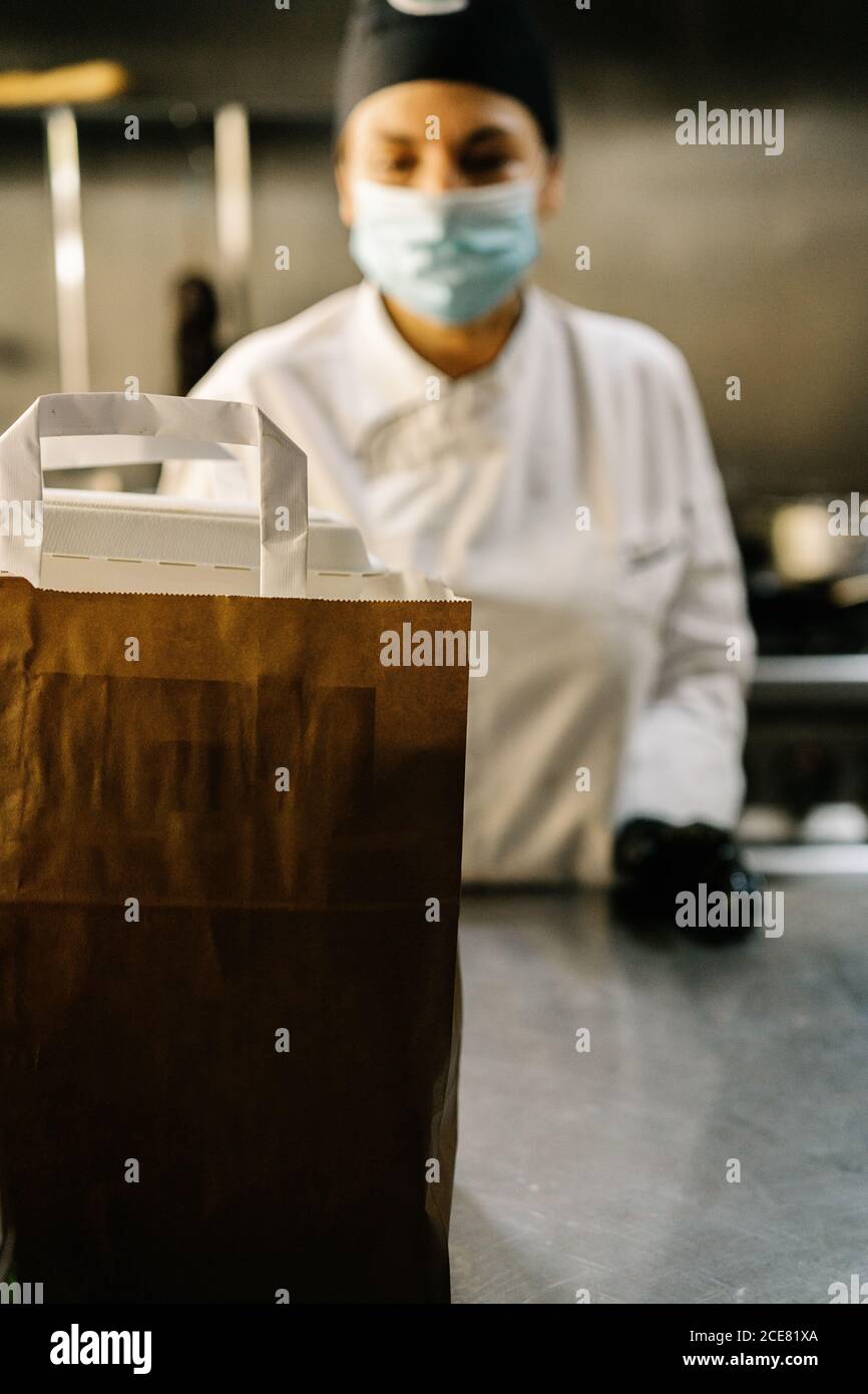 Concentrated female chef wearing face mask and uniform while working in ...
