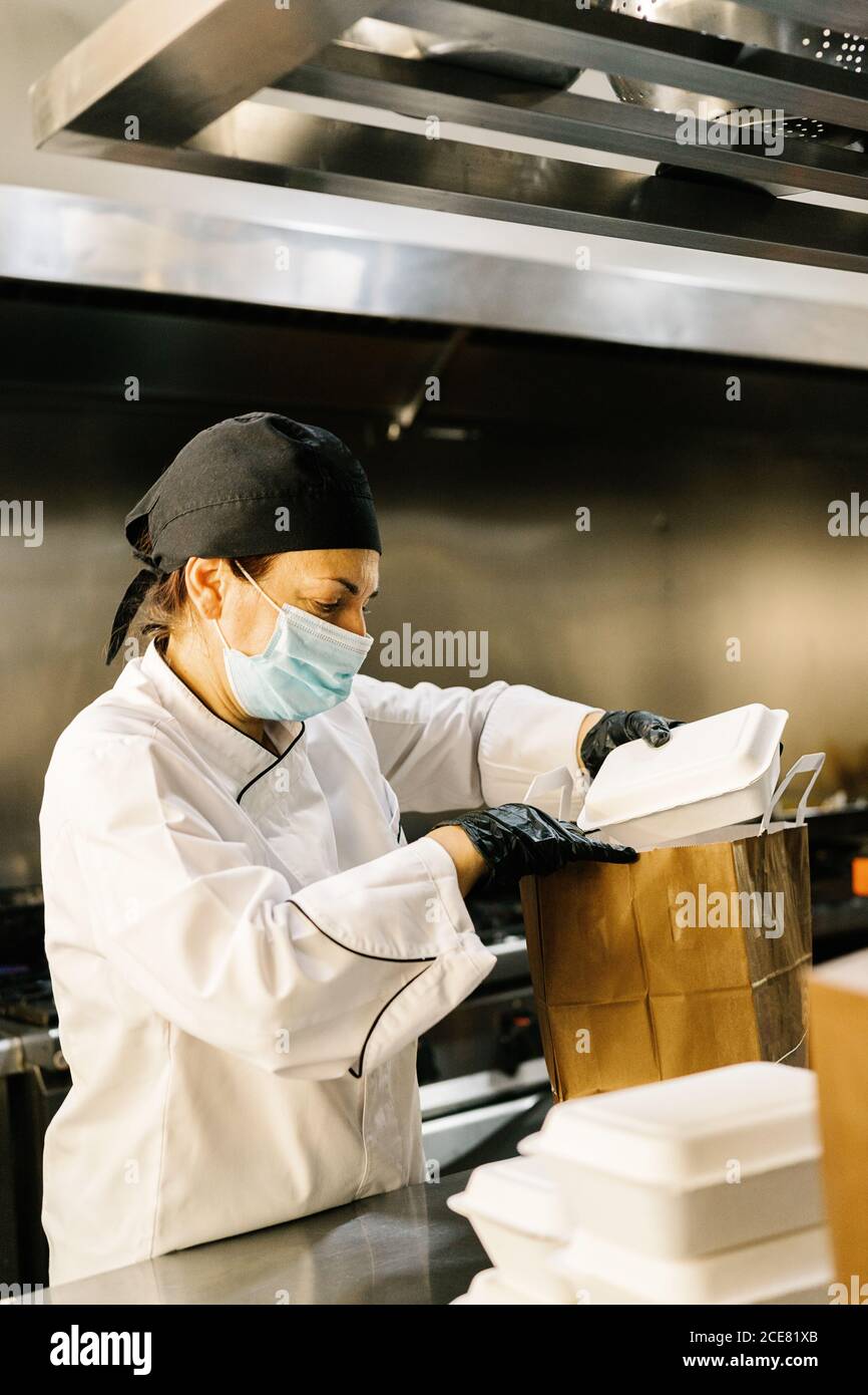 Concentrated female chef wearing face mask and uniform while working in ...