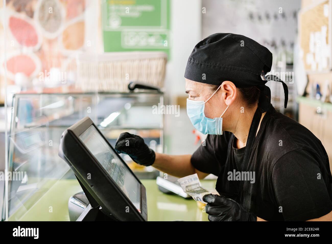 Side view serious female cashier wearing gloves and mask tapping on ...