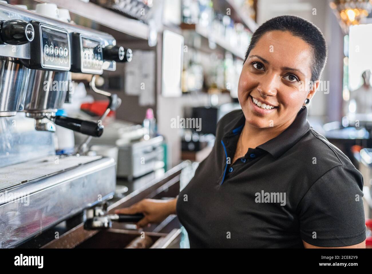 Side view of positive ethnic barista pouring hot coffee into cup from ...