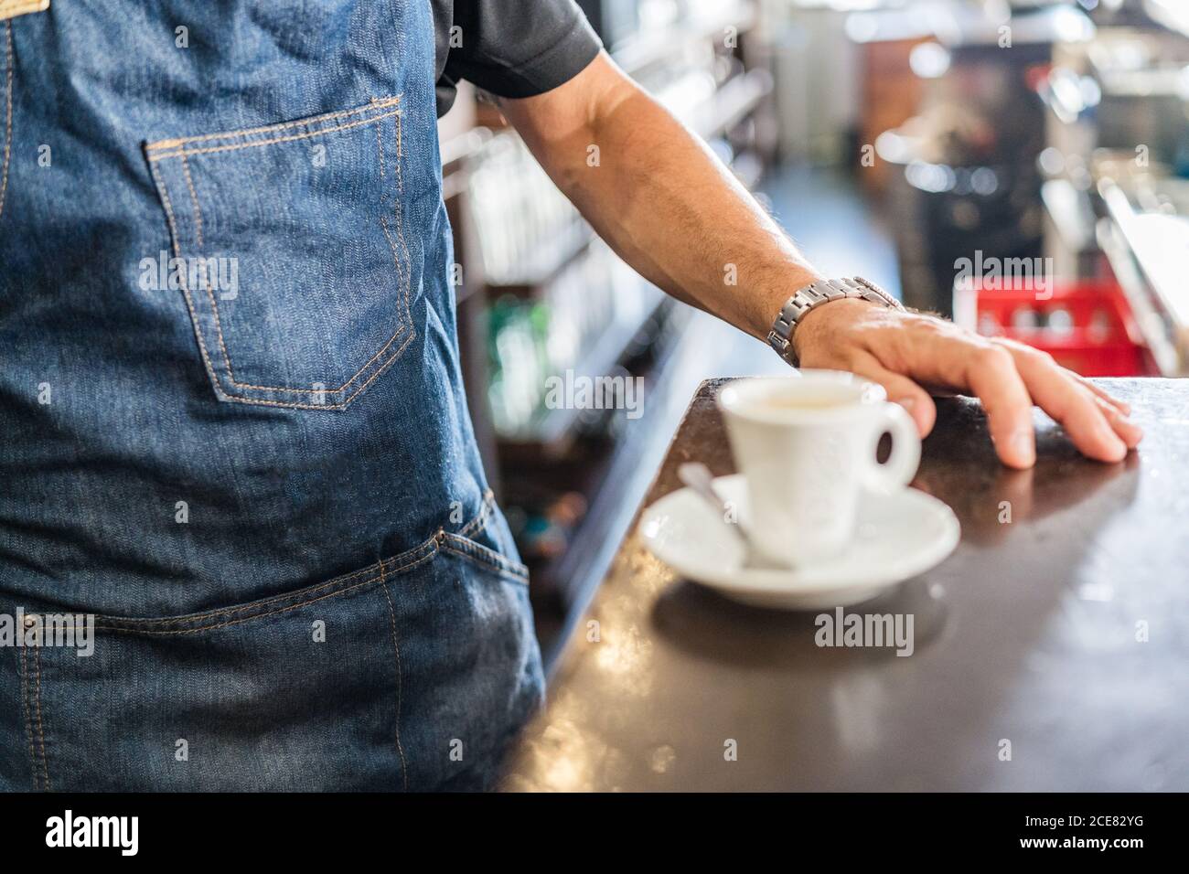 Cropped unrecognziable barista in apron standing at counter with ...