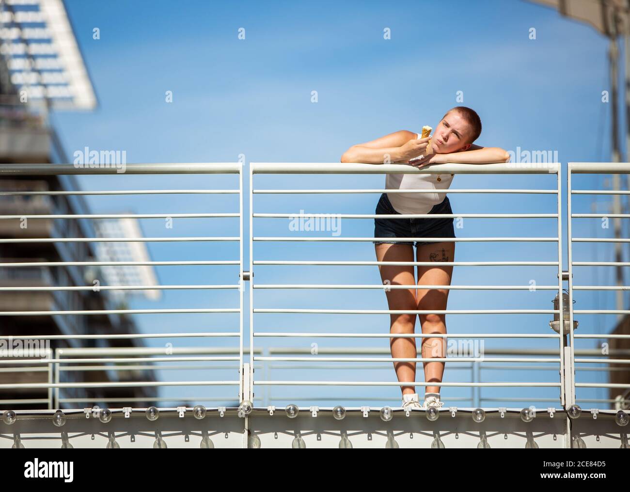 Full body young Woman with shaved head leaning on bridge railing and ...