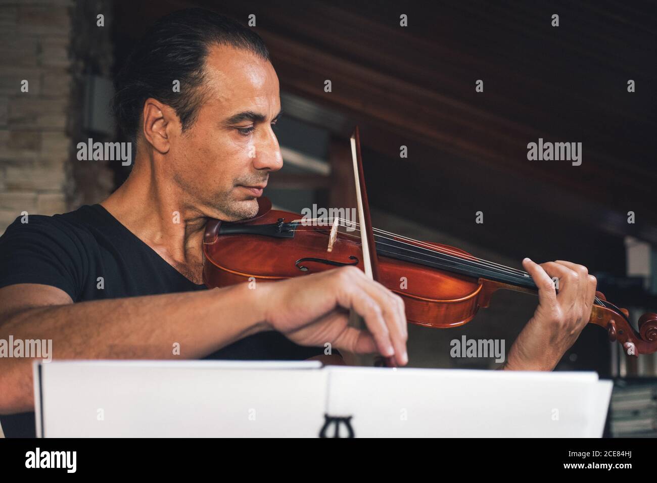 Talented Hispanic male violinist playing violin and looking at music ...