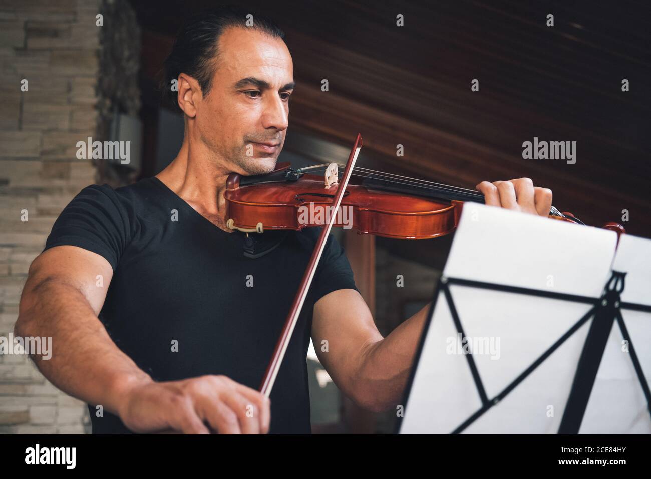 Talented Hispanic male violinist playing violin and looking at music ...