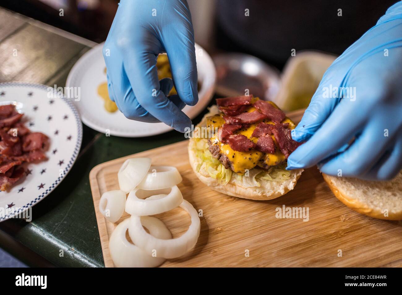 High angle of anonymous chef in medical gloves adding chopped meat on ...