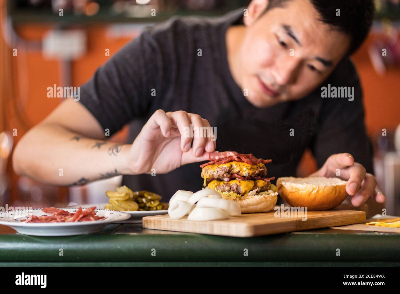 Male chef standing at table and adding meat on tasty cutlet of burger ...