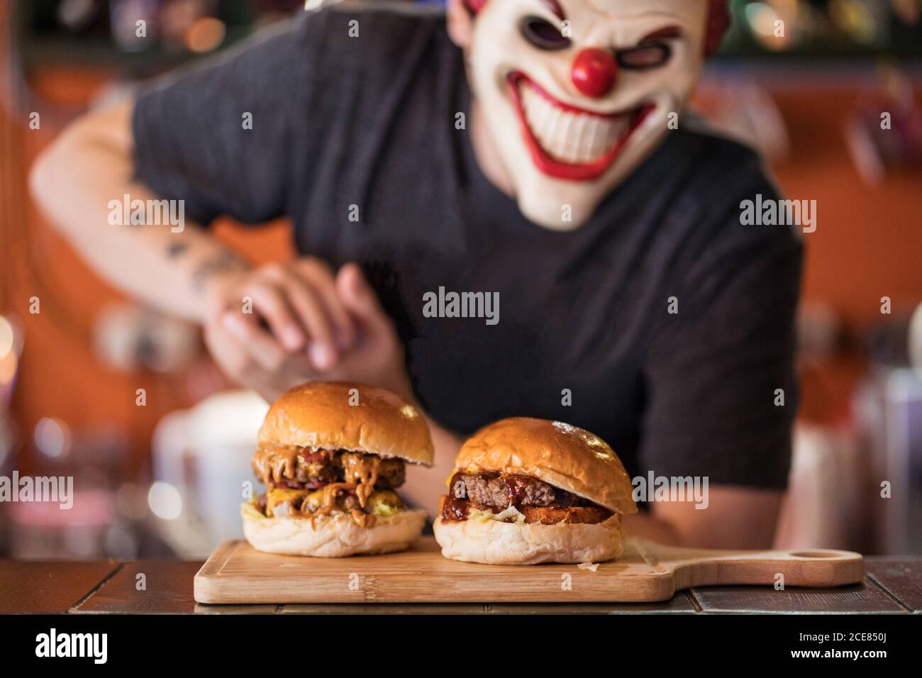 Male chef wearing scary clown mask standing at counter with delicious ...
