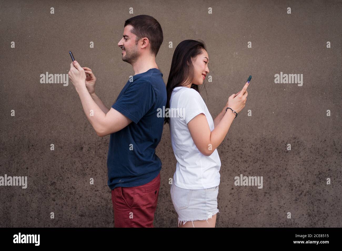 Side view of multiethnic man and Woman standing back to back and using ...