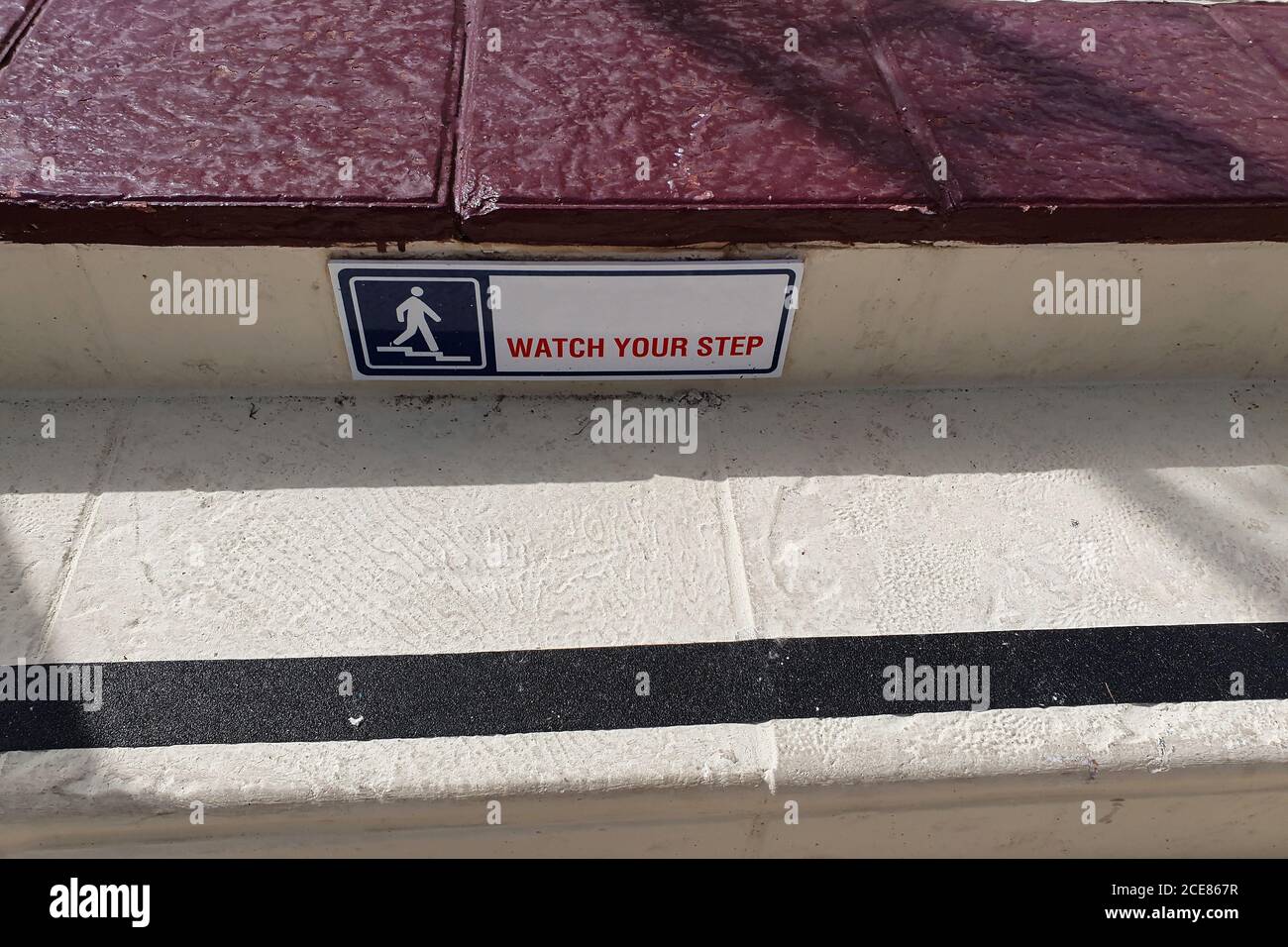 Plate with a reminding sign "Watch your step" and a black strip on the ...