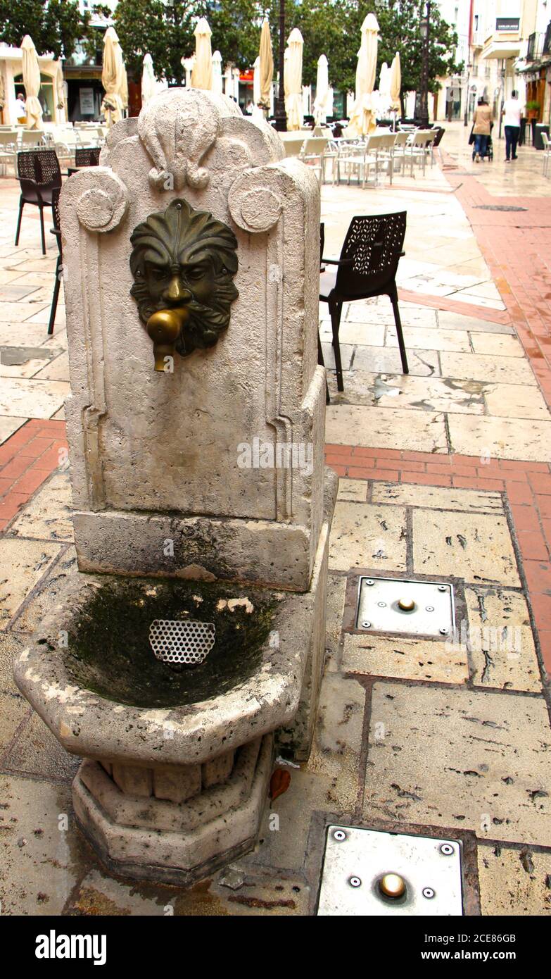 Public water fountain in stone with a brass face and chairs and tables ...