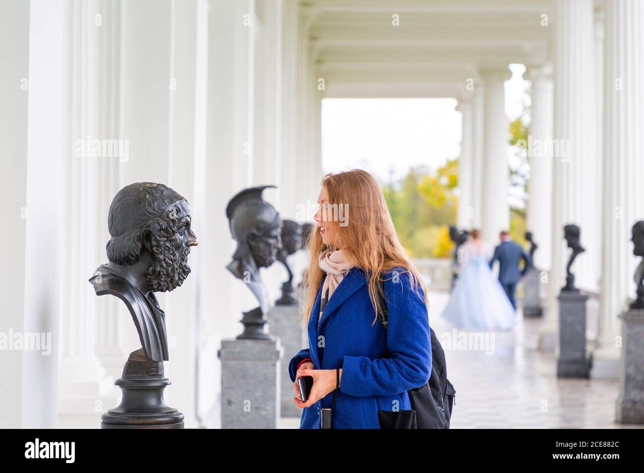 A woman looks at a bronze statue. Side view. In the background is a ...