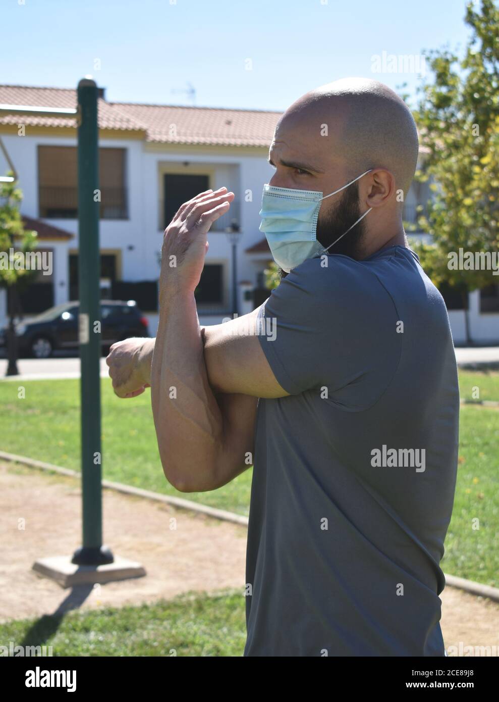 Fitness man doing arms stretching and wearing a face mask in a public ...