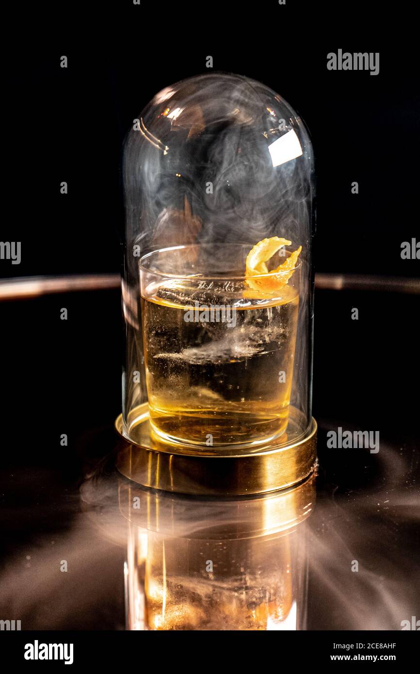 Glass of alcohol drink placed under dome with smoke on reflective table ...