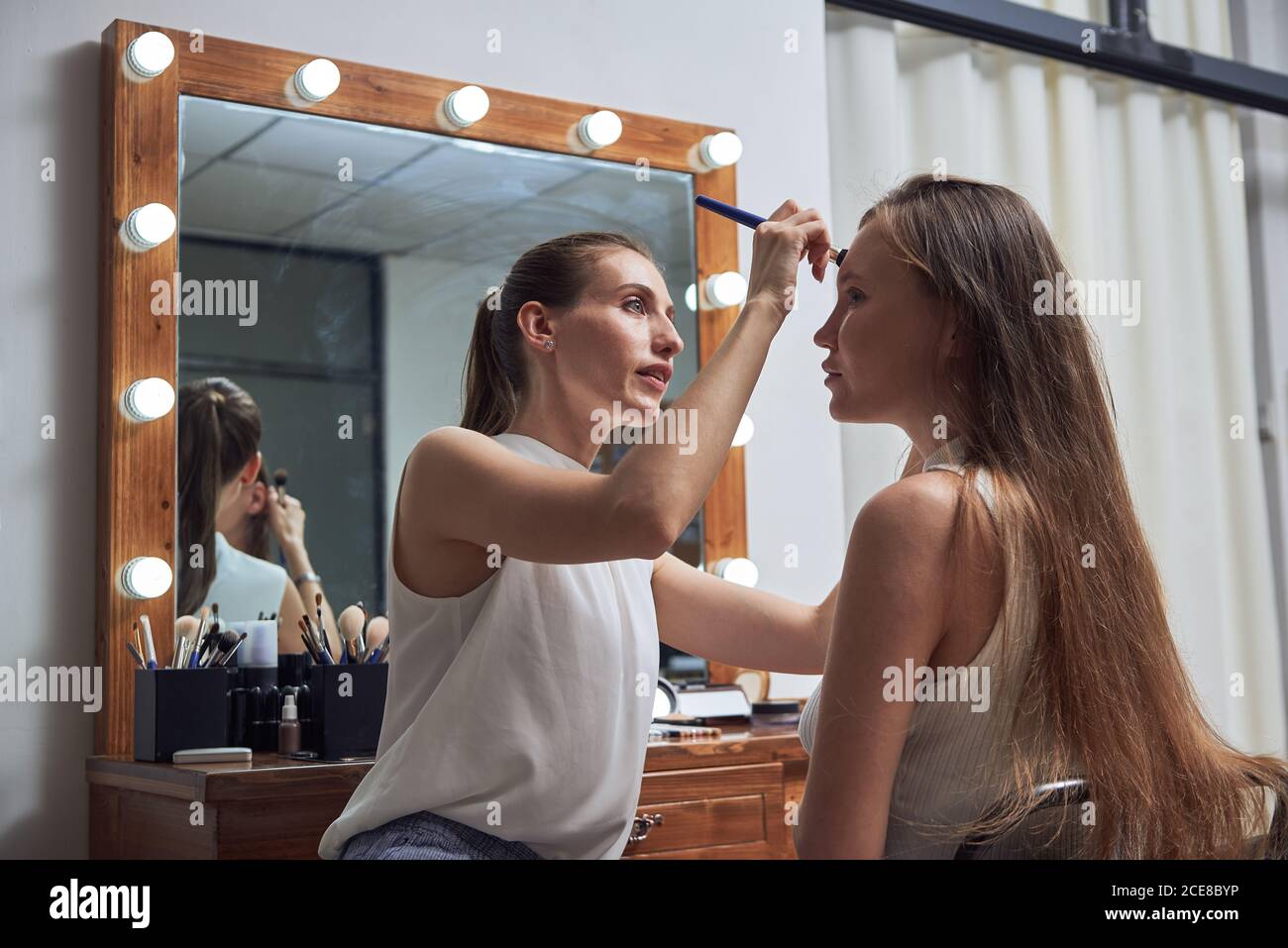 Positive young female makeup artist doing clients face makeup using ...