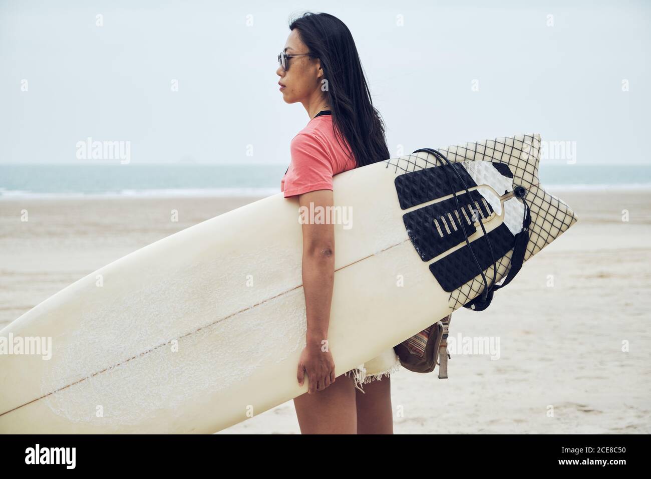 Side view of young Asian female surfer in summer outfit walking on ...