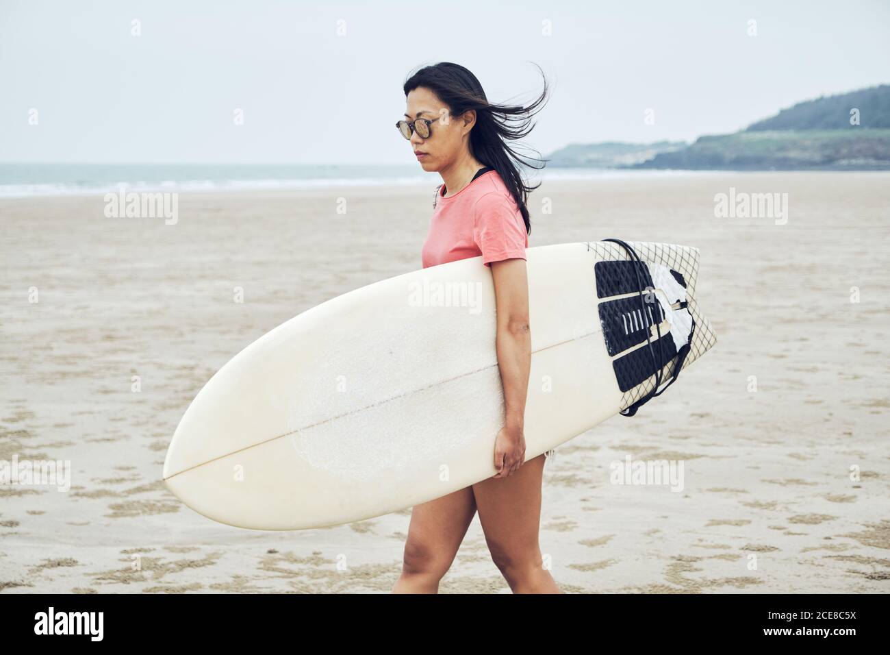 Side view of young Asian female surfer in summer outfit walking on ...