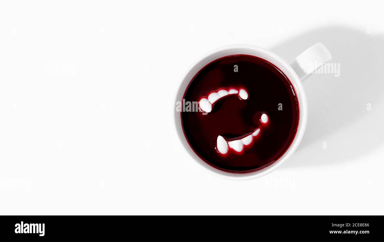 White cup with fake blood and toy vampire teeth on white background ...