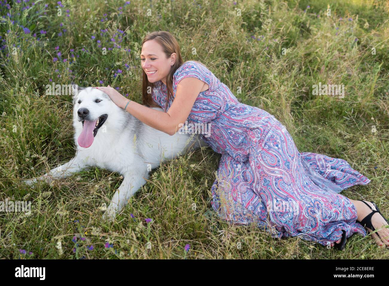 Delighted female in summer dress and straw hat relaxing on meadow with ...