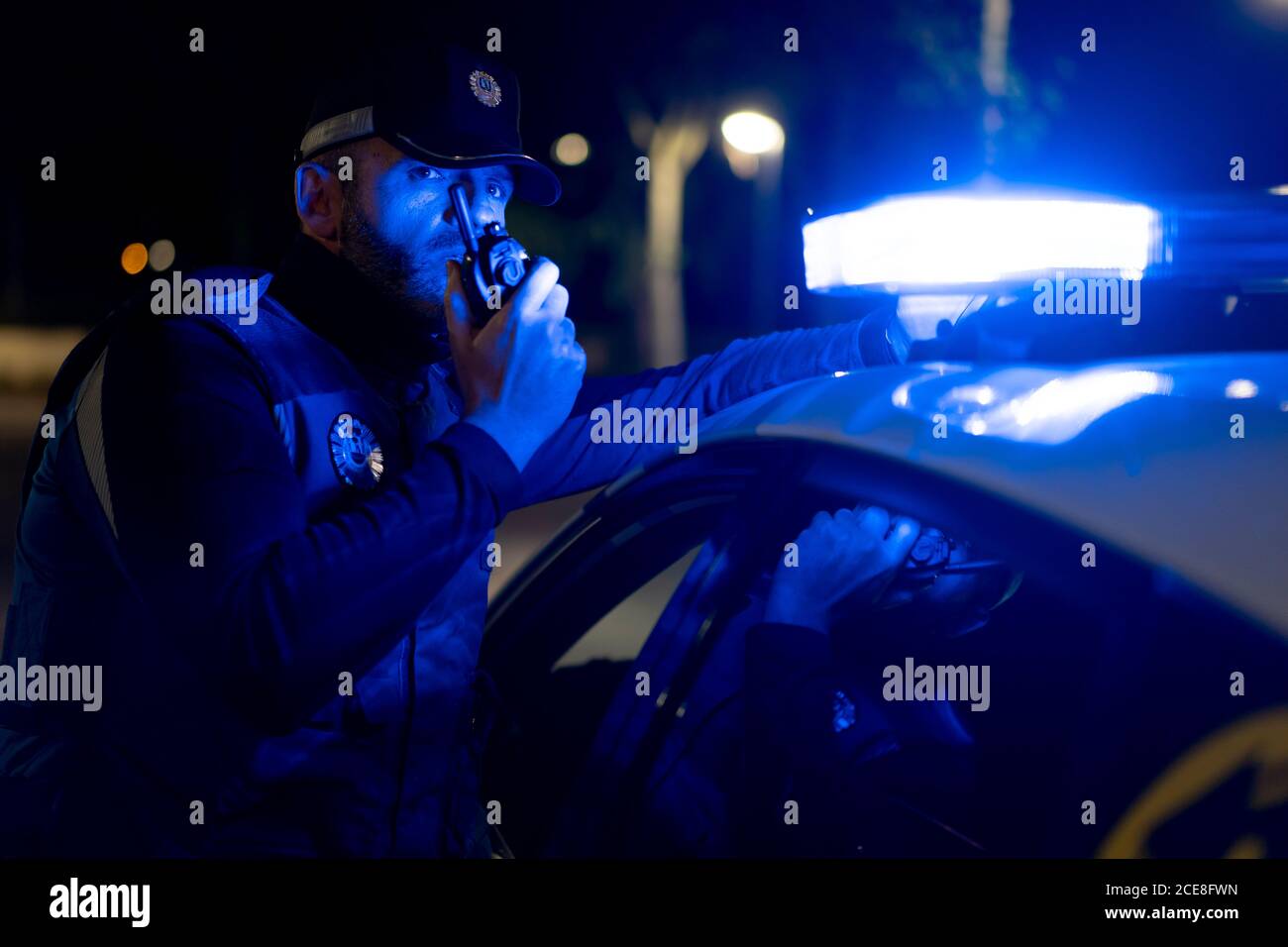 Serious male police officer in uniform standing near automobile with ...