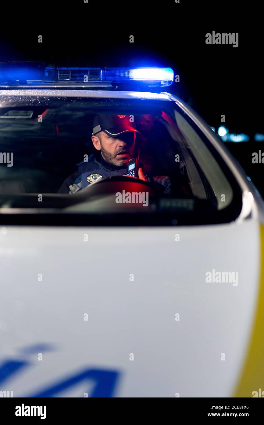 Male police officer sitting in parked automobile with siren light Stock ...