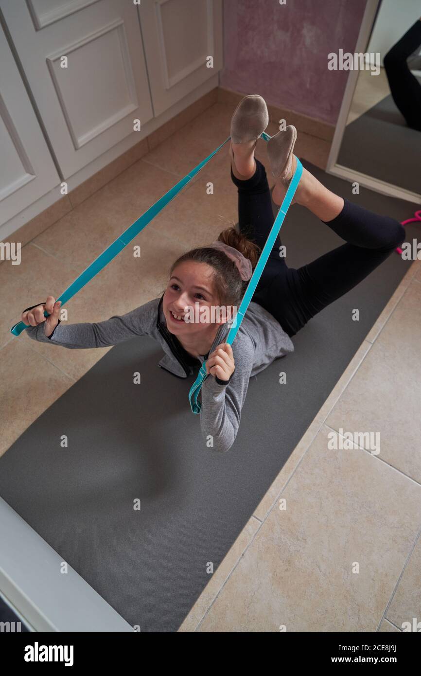 From above girl doing bow pose with elastic band while stretching spine ...