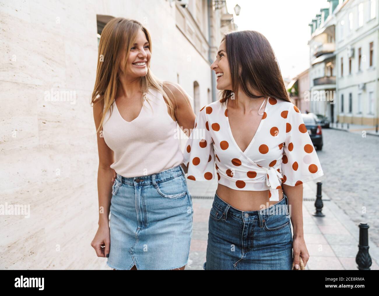 Image of cheerful adult two women hugging and laughing while walking on ...
