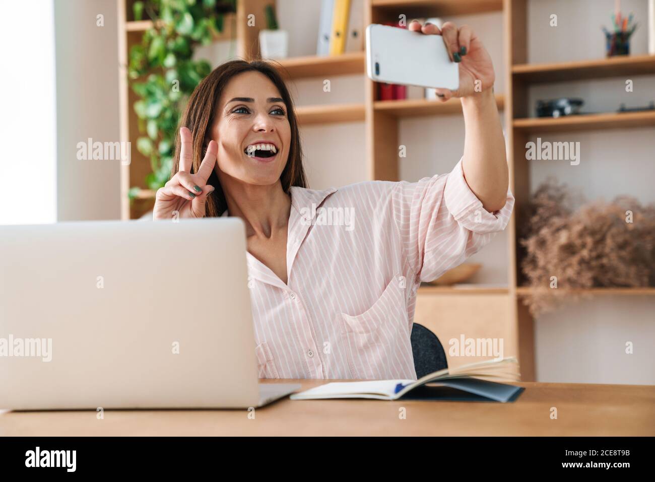 Image of happy adult businesswoman gesturing peace sign and taking ...